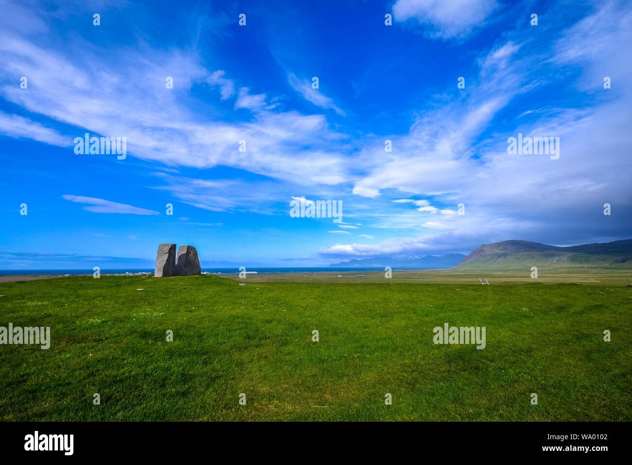 Grassy field with two big rocks in the distance under a cloudy sky ...
