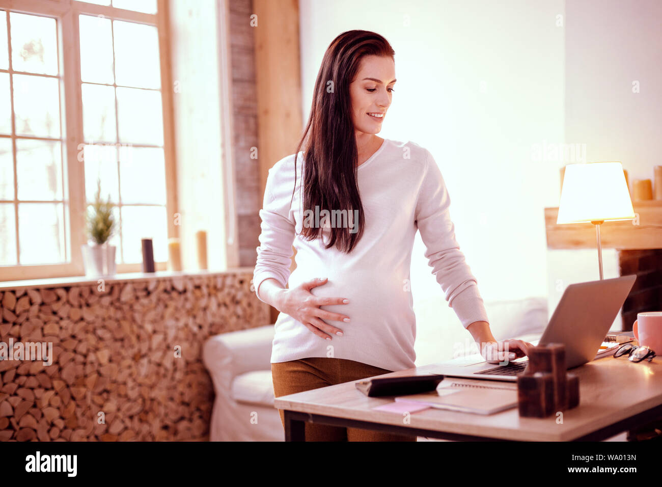 Keep smiling. Beautiful young woman keeping smile on her face while caressing her baby bump ...