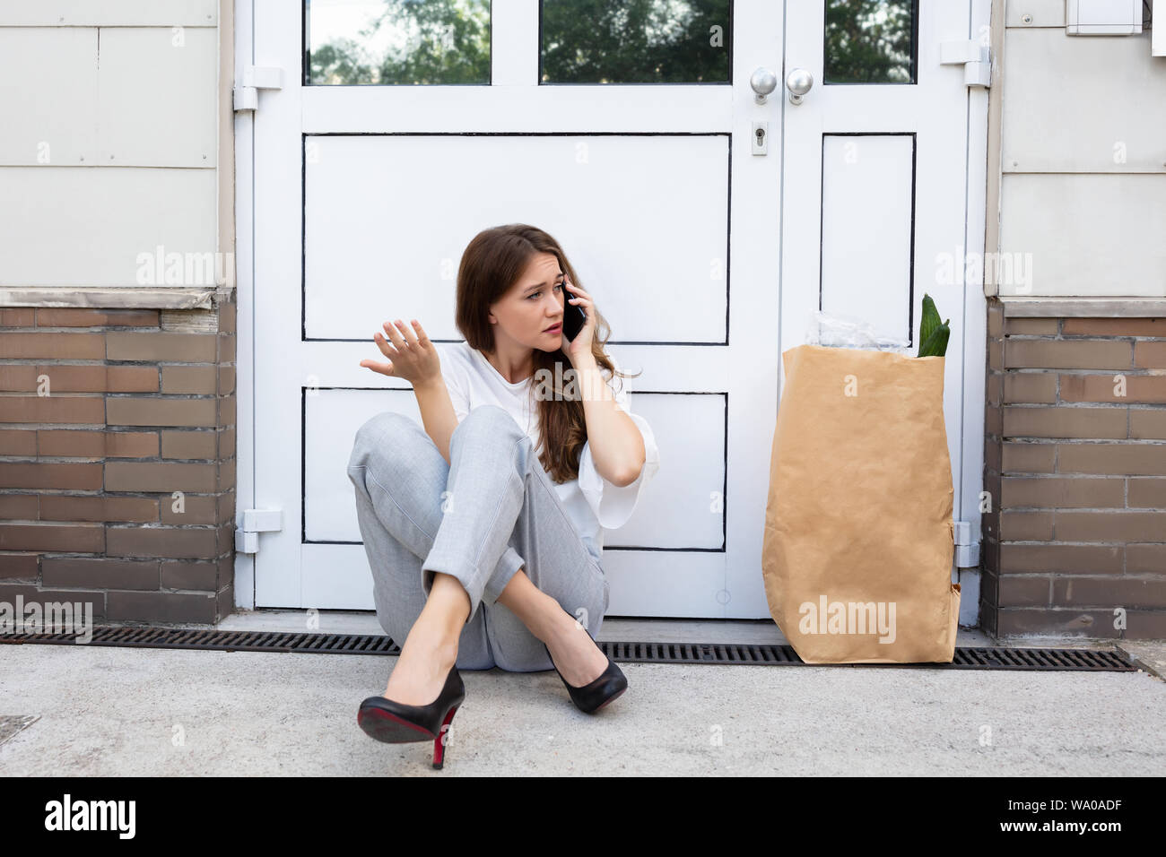An Afraid Young Woman Sitting Outside The Door Talking On Mobilephone ...