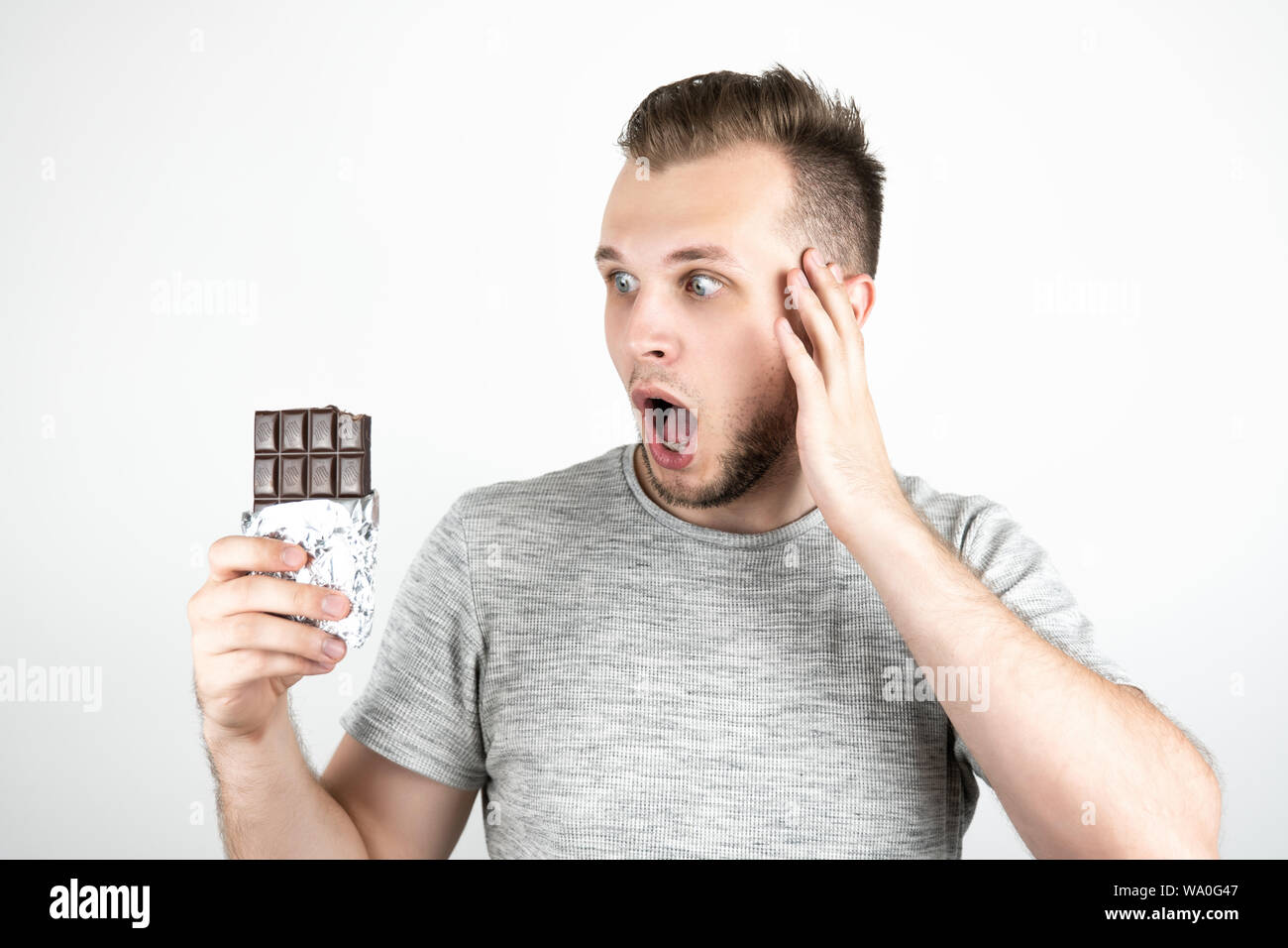 young handsome man holding chocolate bar looking surprised on isolated ...