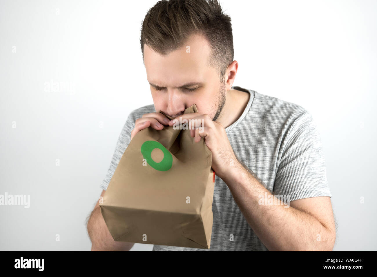 young man vomiting in paper bag after eating fast food snacks on ...