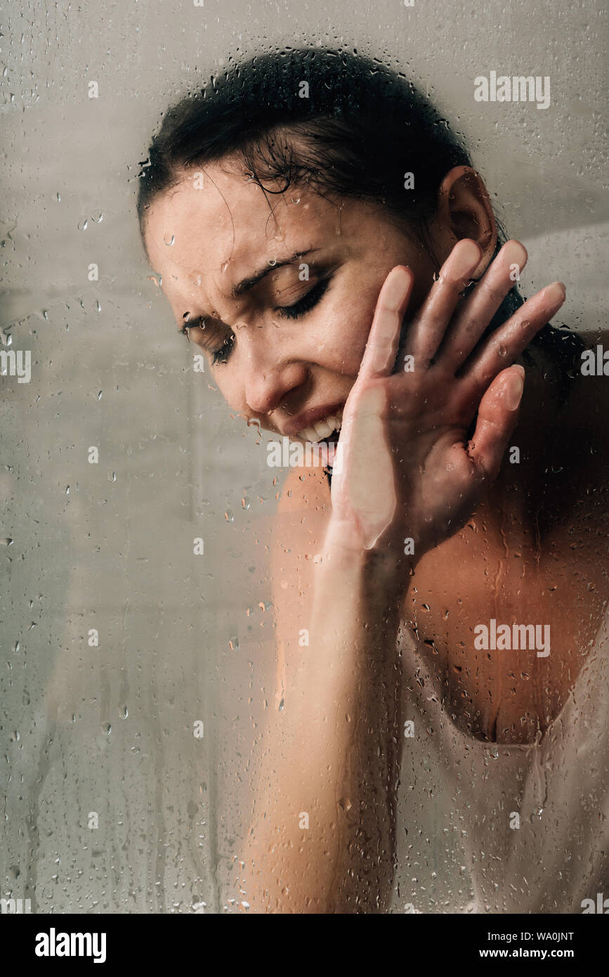 lonely depressed woman crying in shower through glass with water drops ...