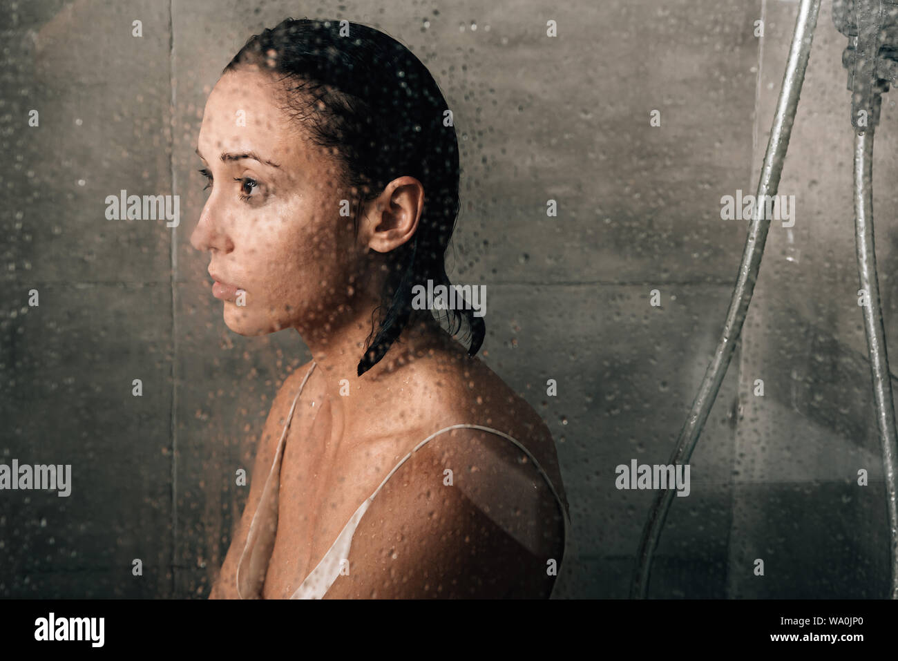 beautiful sad woman in shower at home through glass with water drops ...