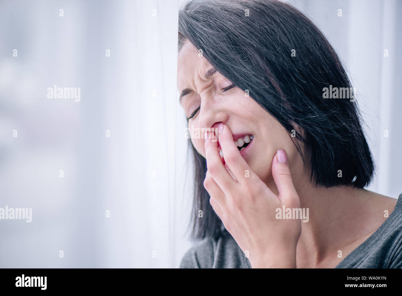 selective focus of depressed brunette woman covering mouth and crying ...