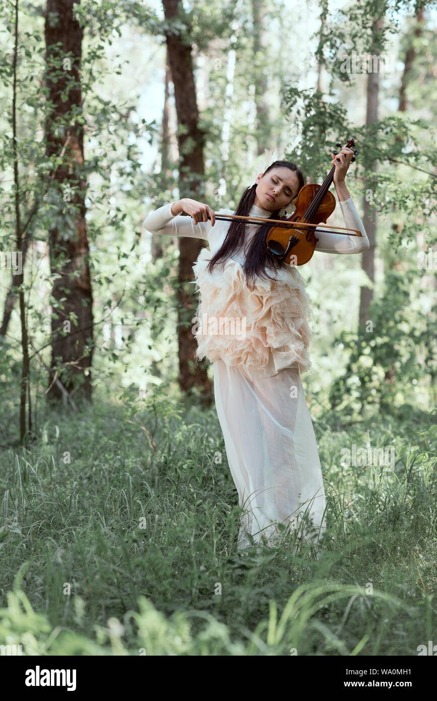 tender woman in white swan costume standing on forest background with ...