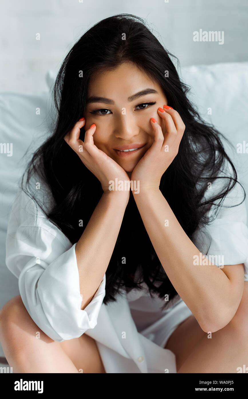 happy thai woman smiling at touching face while looking at camera and ...