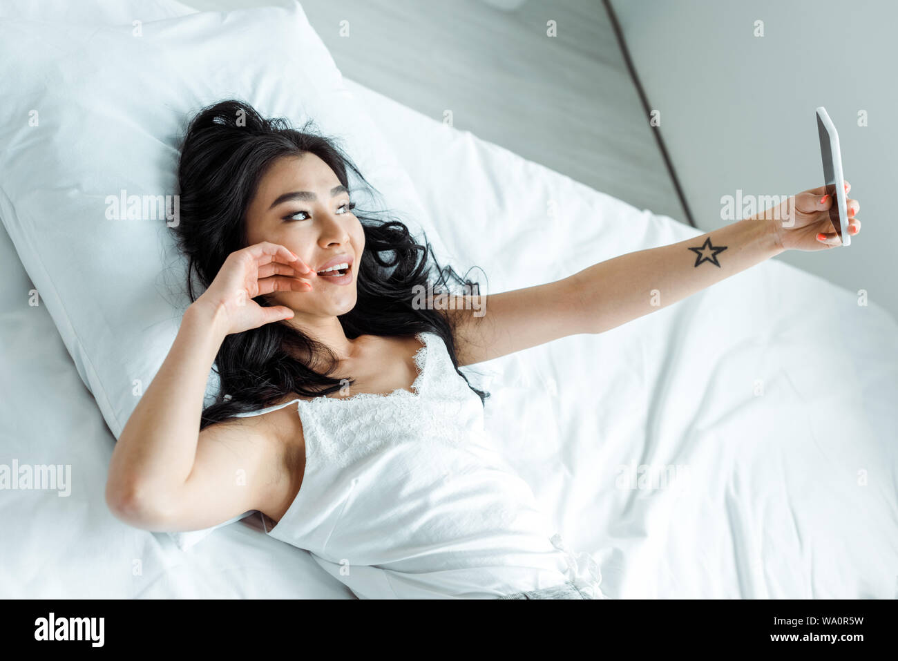overhead view of asian girl taking selfie on smartphone while lying on ...