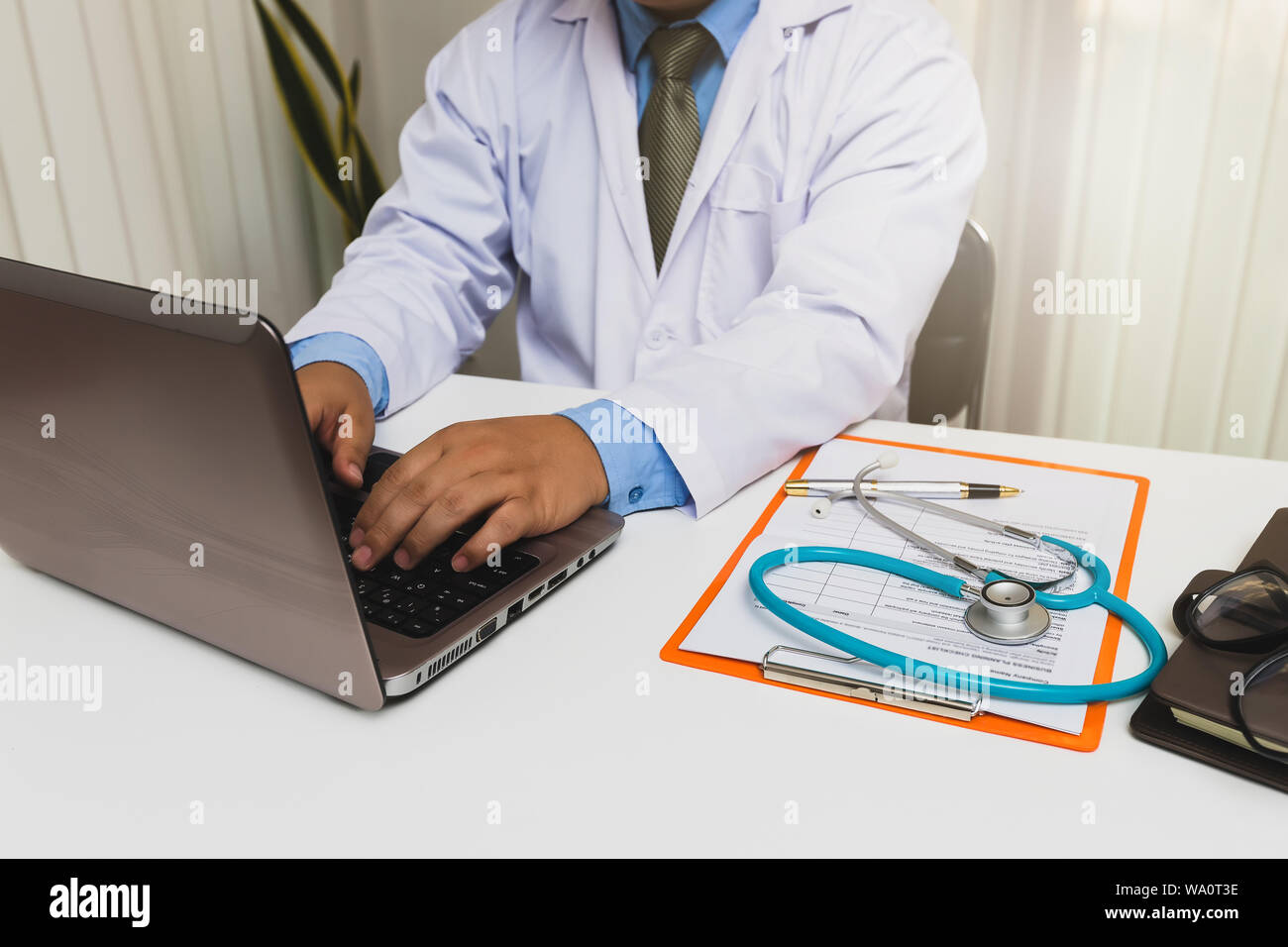 doctor sitting at the table near the window in hospital and typing at ...