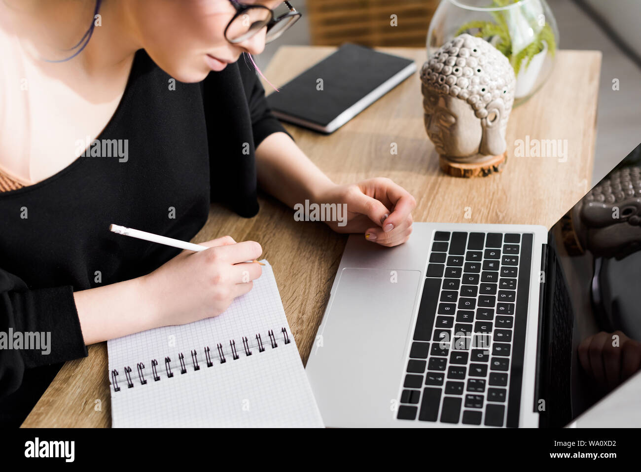 beautiful girl sitting behind table with laptop and writing in notebook ...