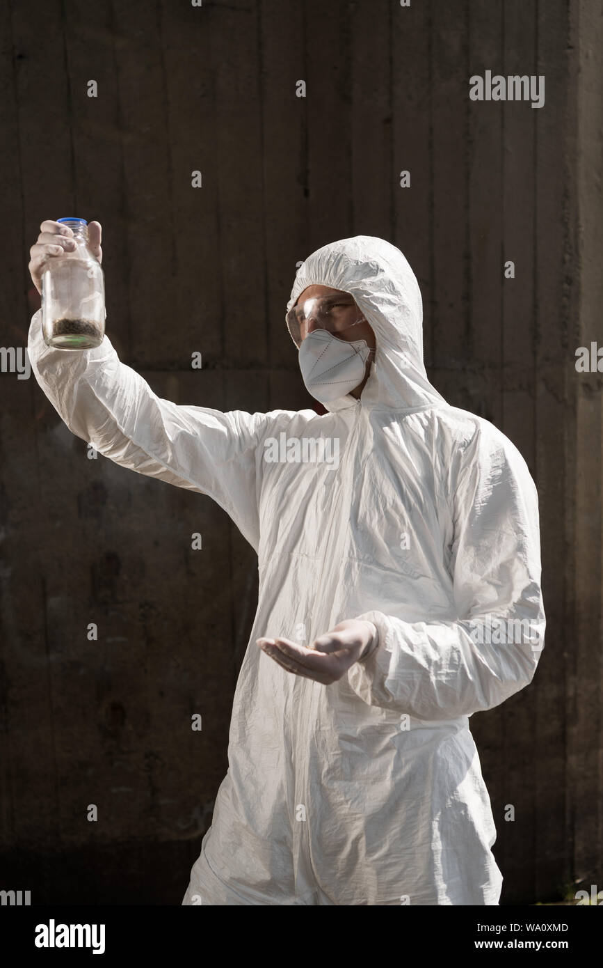 ecologist in protective costume and respirator holding bottle with soil ...