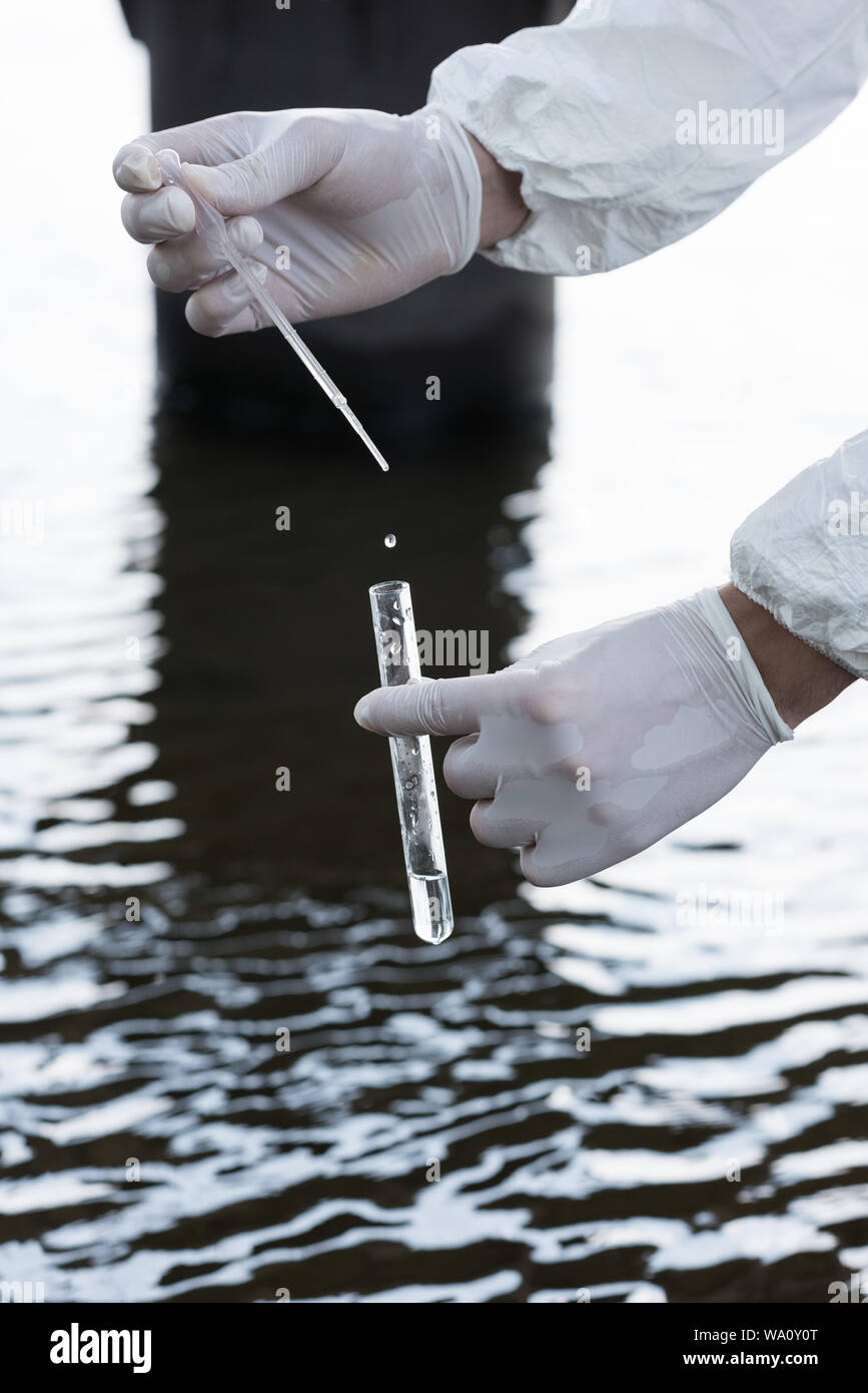 cropped view of water inspector in latex gloves taking water sample at ...