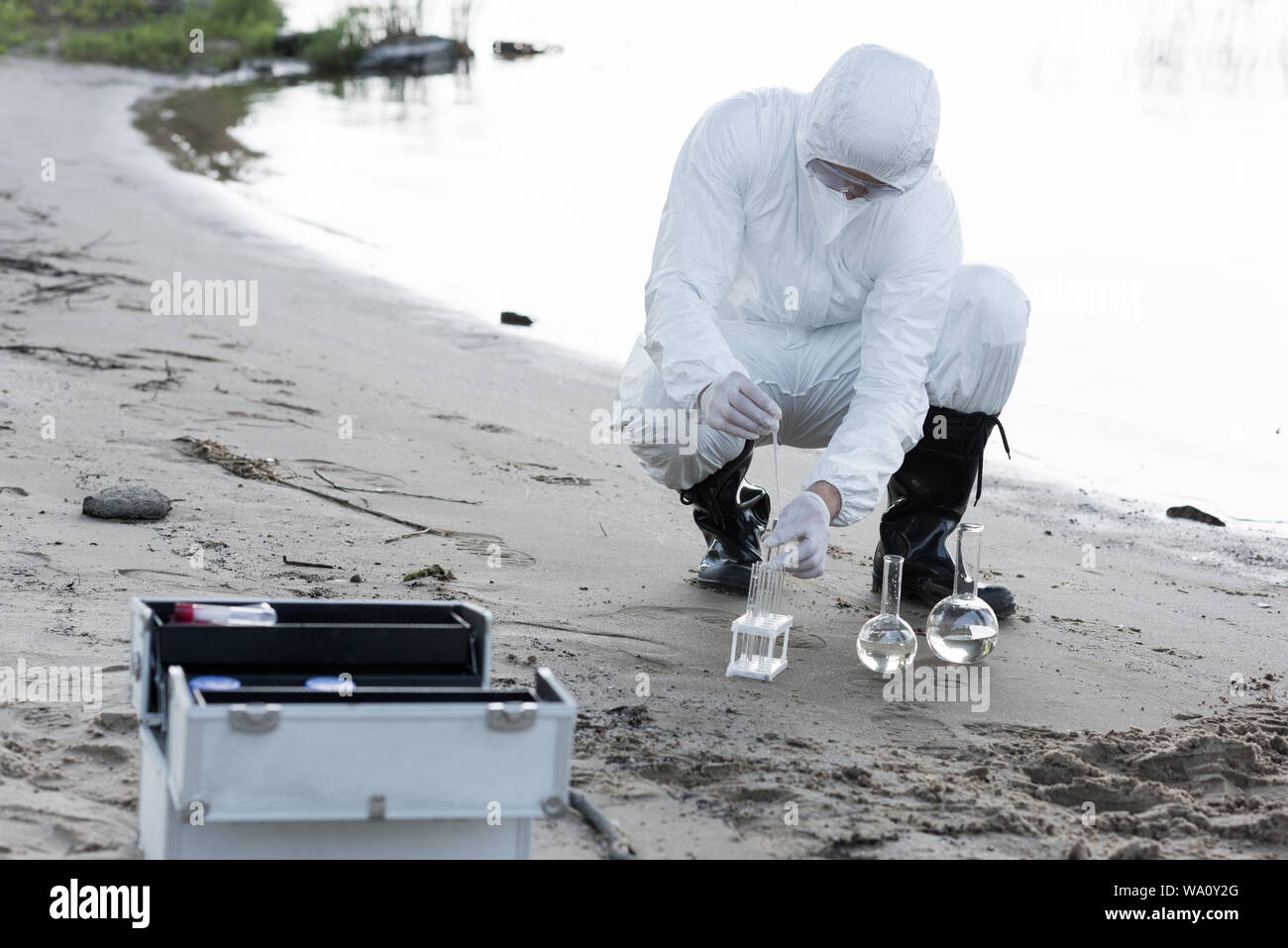 water inspector in protective costume and respirator taking water ...