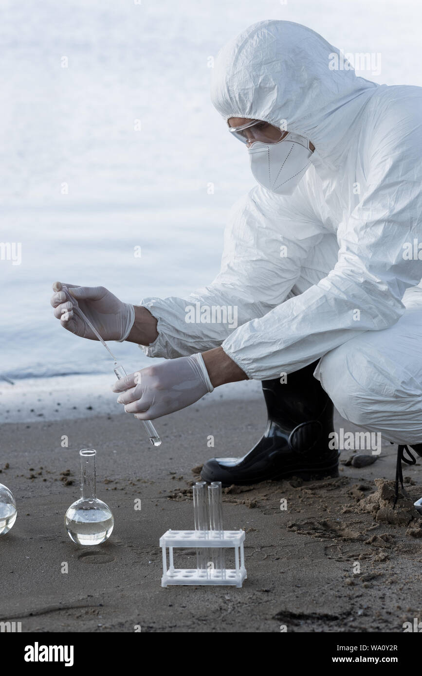 water inspector in protective costume and respirator taking water ...