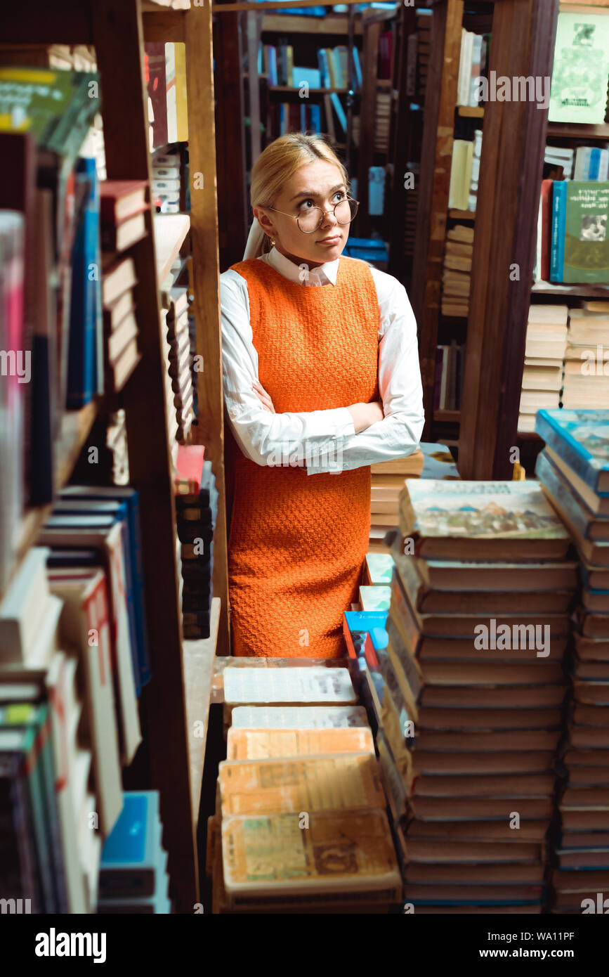 pretty and sad woman in glasses and orange dress with crossed arms ...