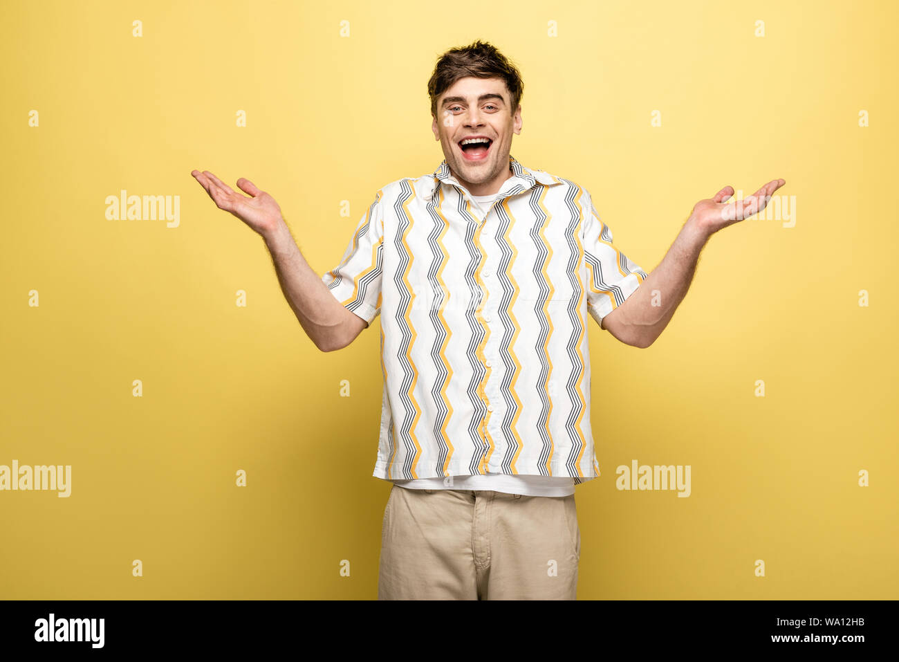 cheerful young man showing shrug gesture and smiling at camera on ...