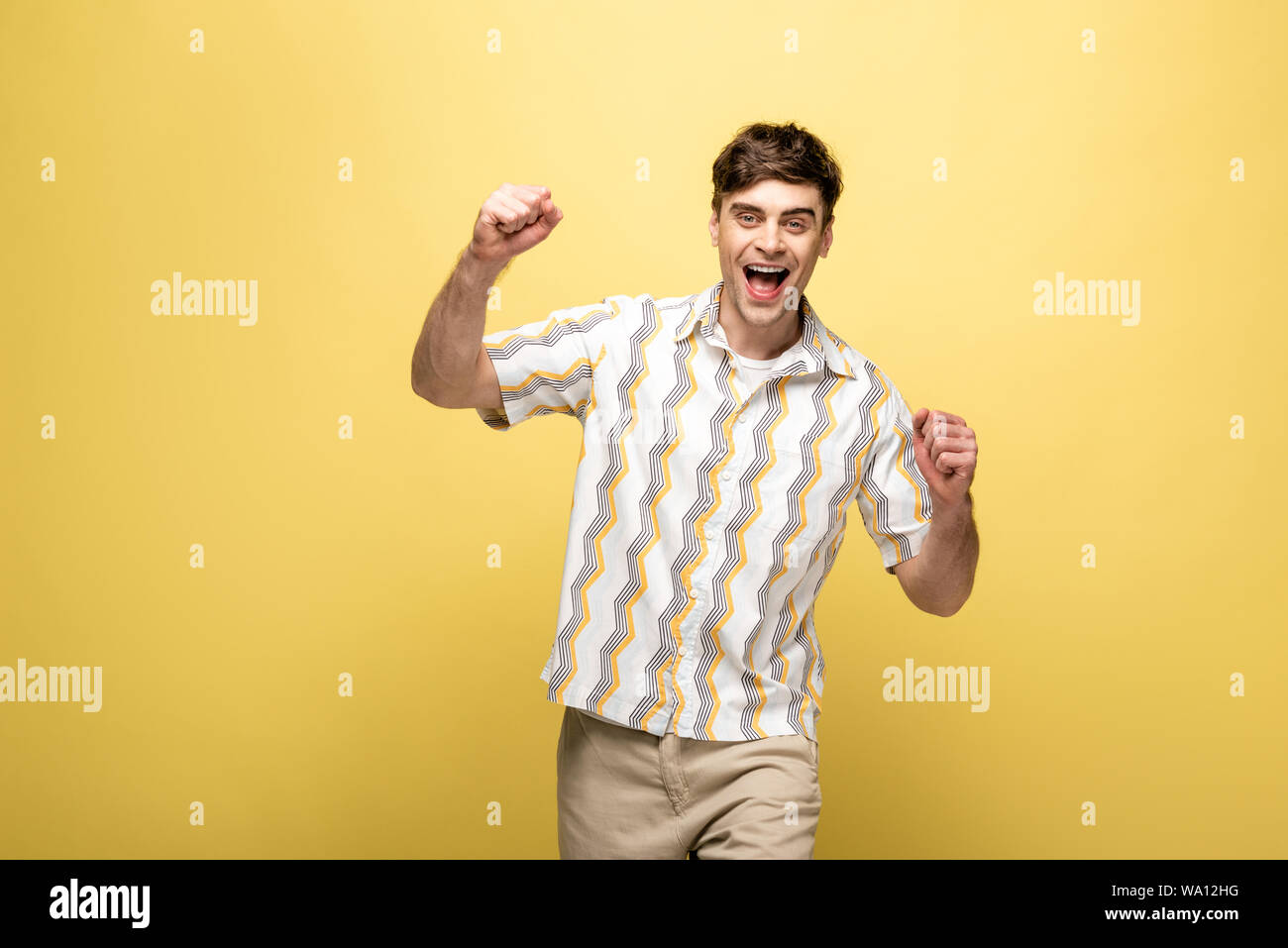 happy man showing winner gesture while smiling at camera on yellow ...
