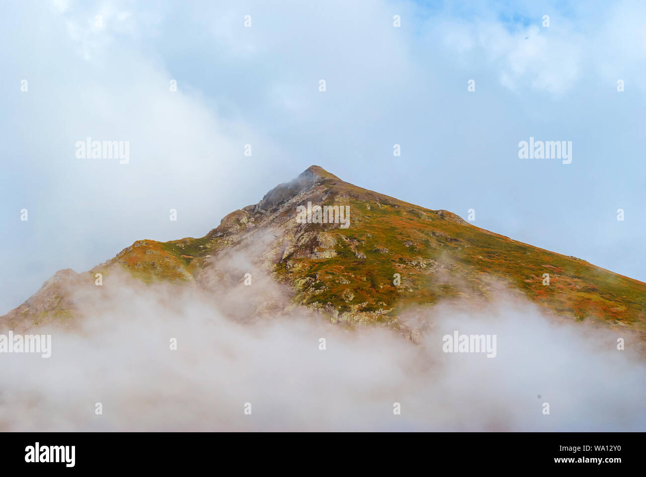 cone-shaped rocky mountain peak with multi-colored vegetation visible ...