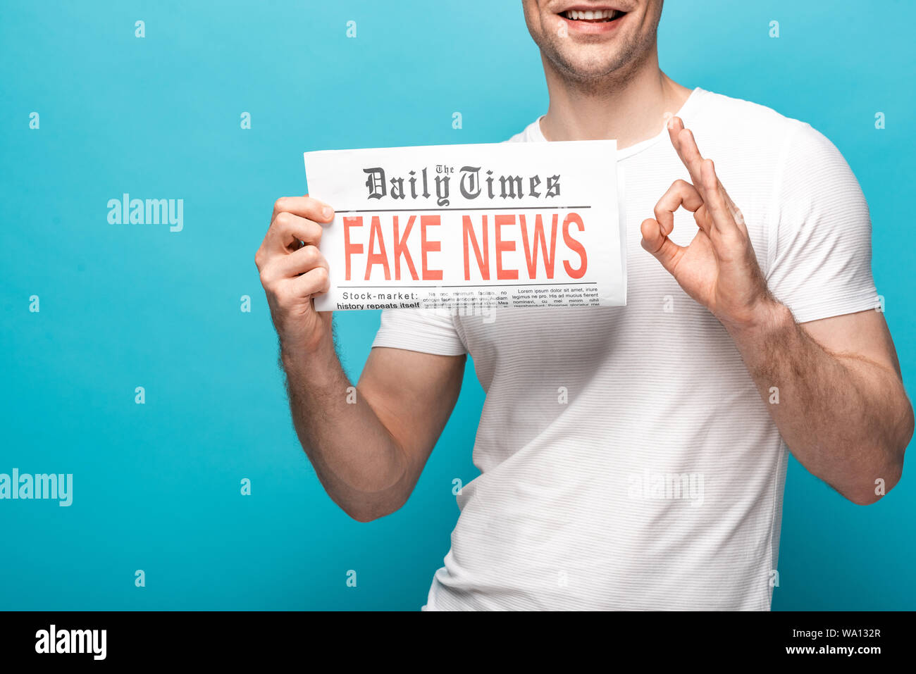 cropped view of smiling man showing ok sign while holding newspaper ...