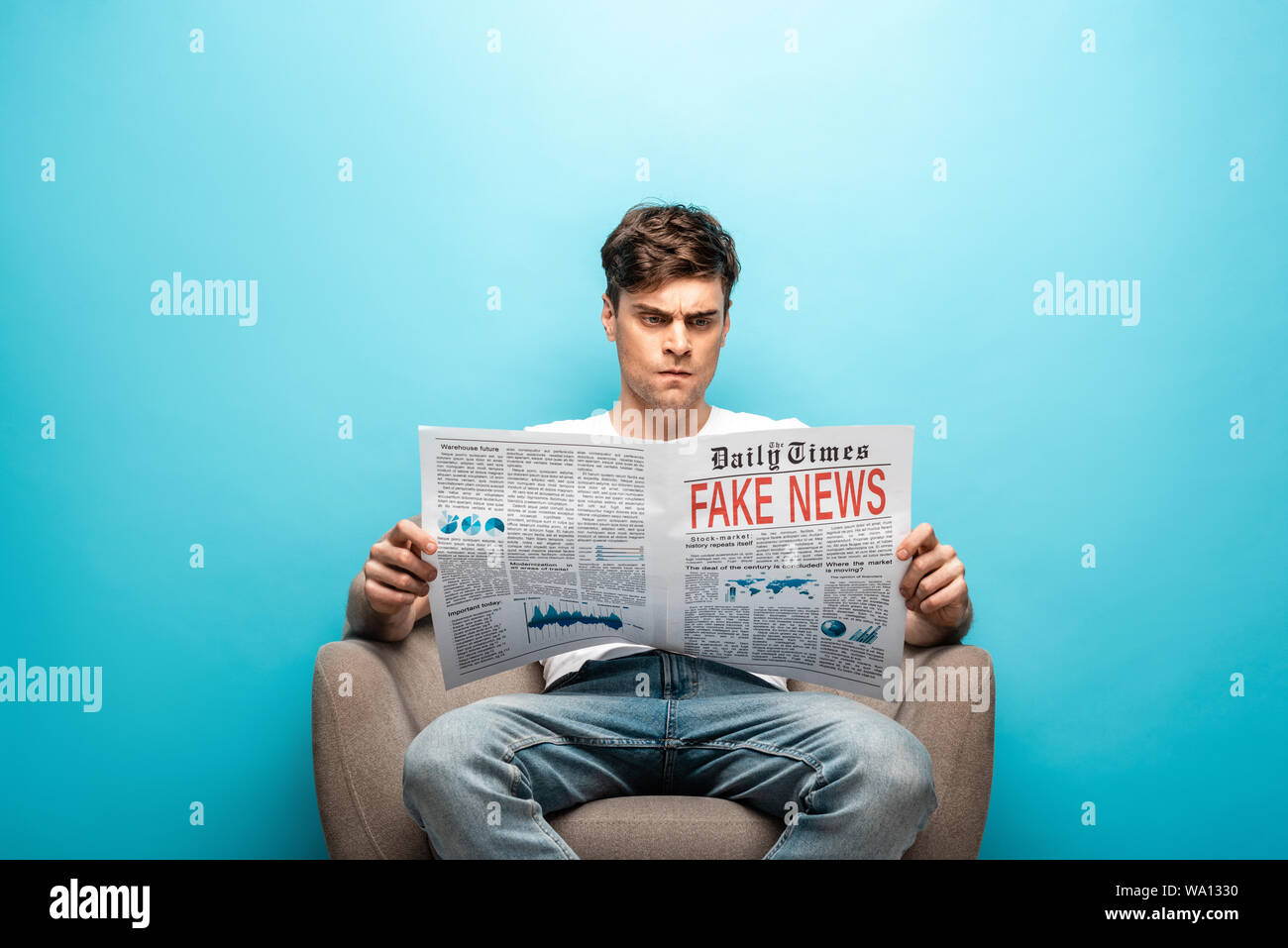 angry young man reading newspaper with fake news while sitting in ...