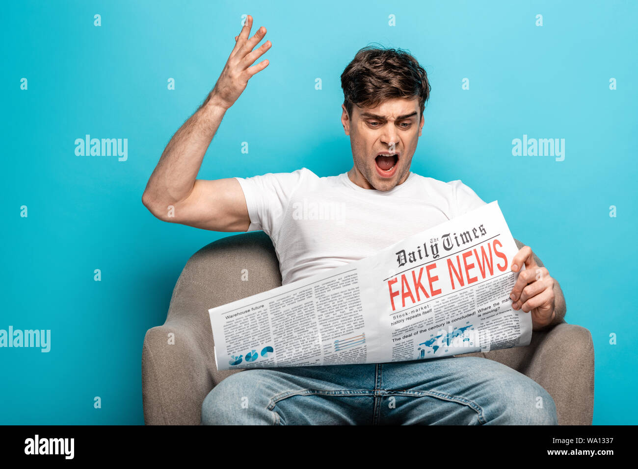 angry man gesturing while sitting in armchair and reading newspaper ...