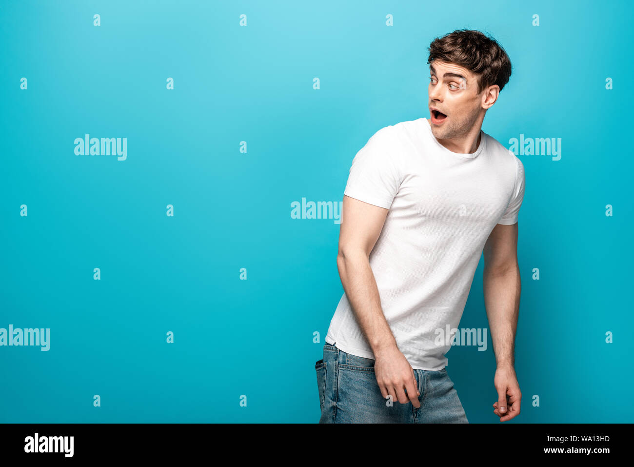 scared young man in white t-shirt looking back on blue background Stock ...