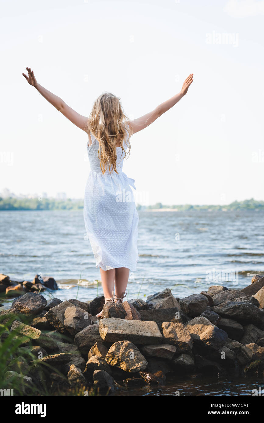 back view of girl in white dress standing on rocky river shore with hands in air Stock Photo - Alamy