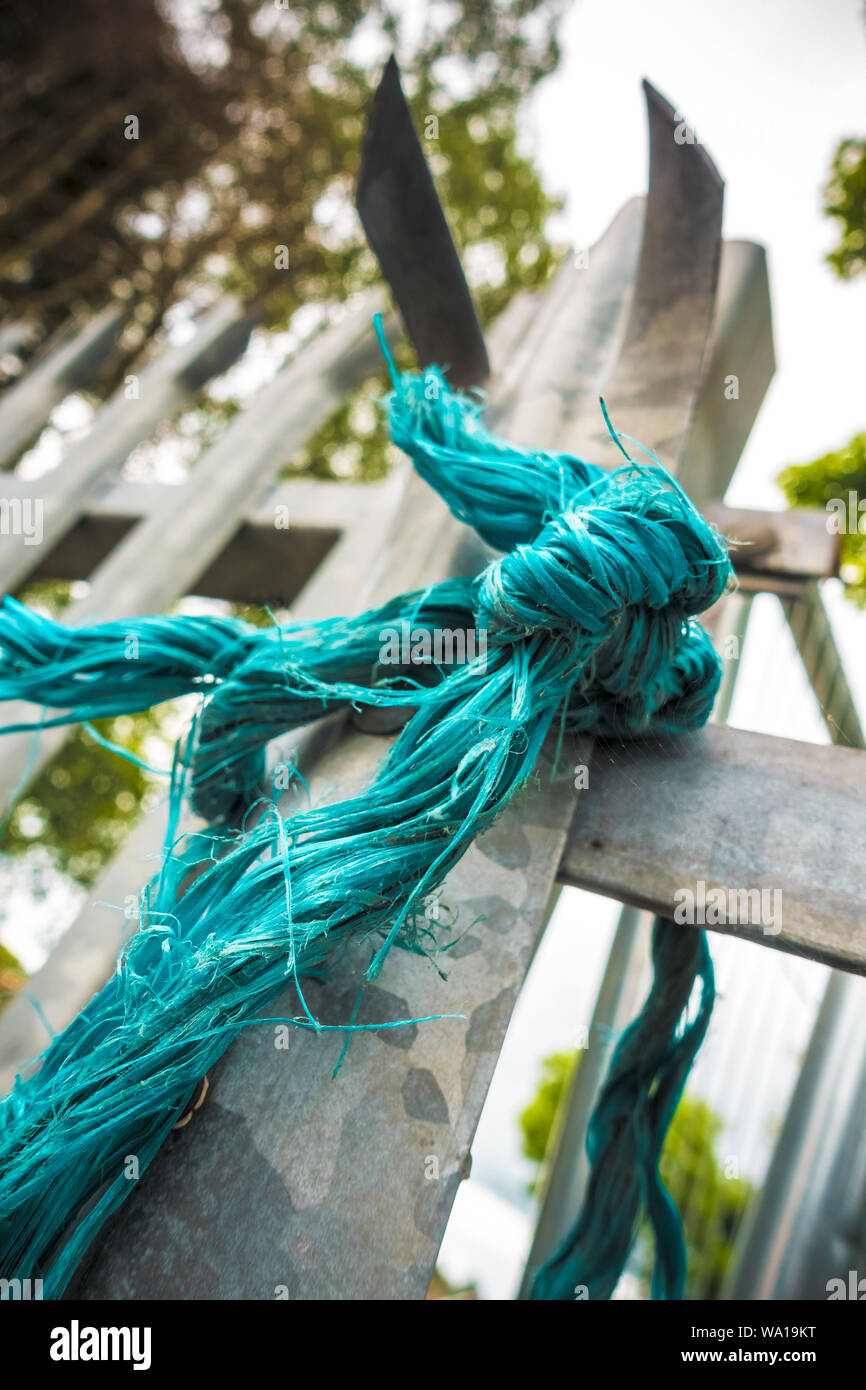 Blue nylon rope knotted and tied to a security fence with spikes on top ...