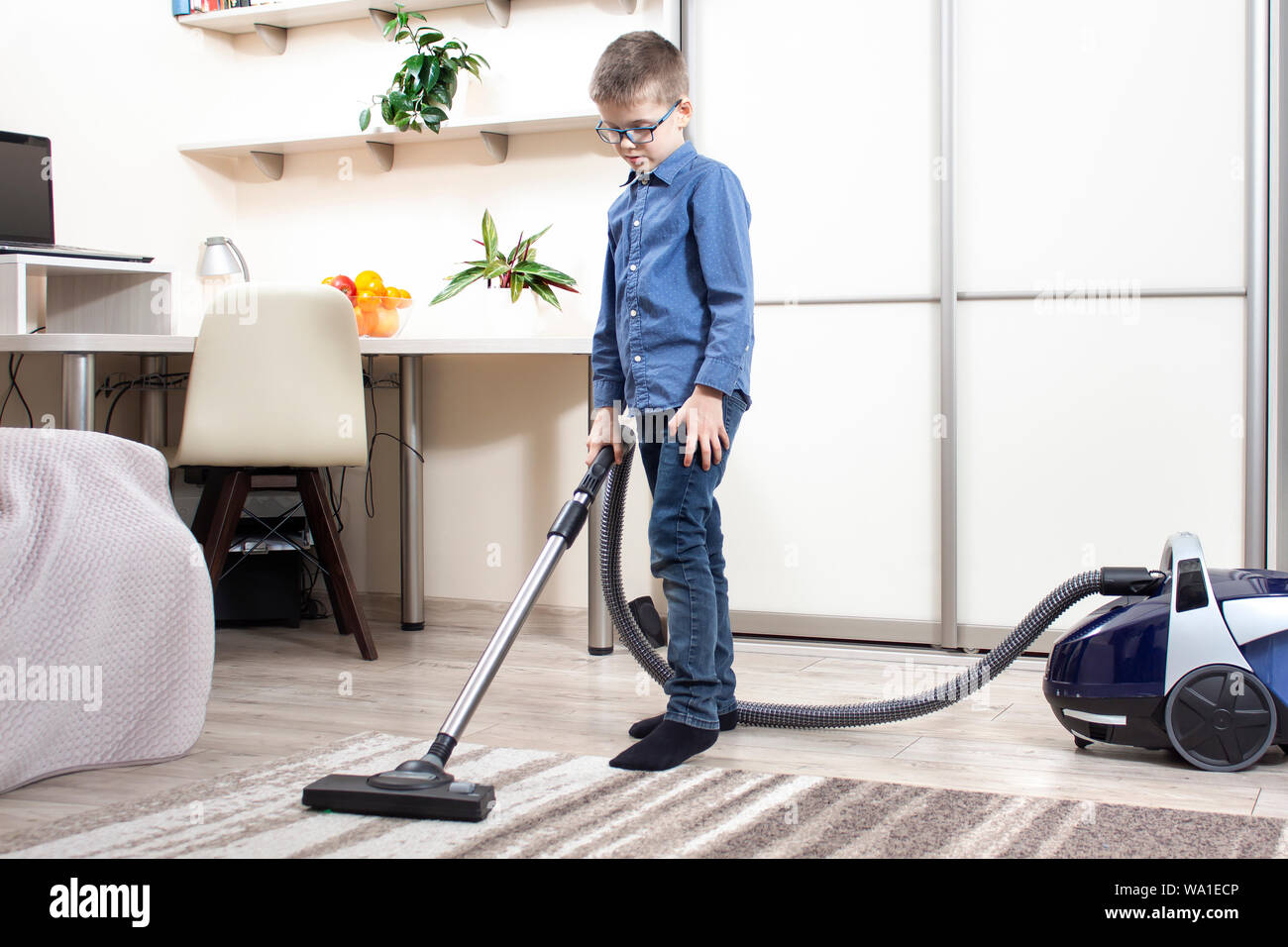 The boy in the glasses cleans the room. Vacuuming the carpet with a ...