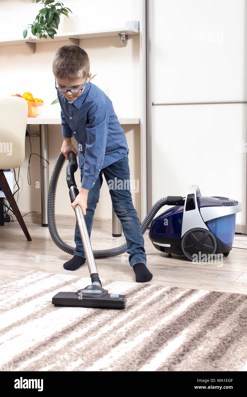 The boy in glasses and a blue shirt is cleaning the flat. Vacuuming the ...