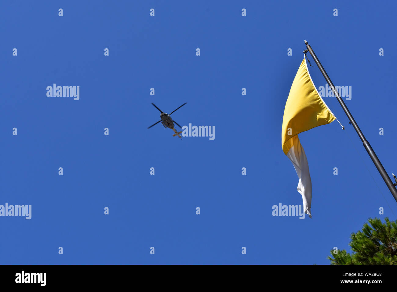 Flying helicopter in the blue sky with white and yellow flag waving in ...