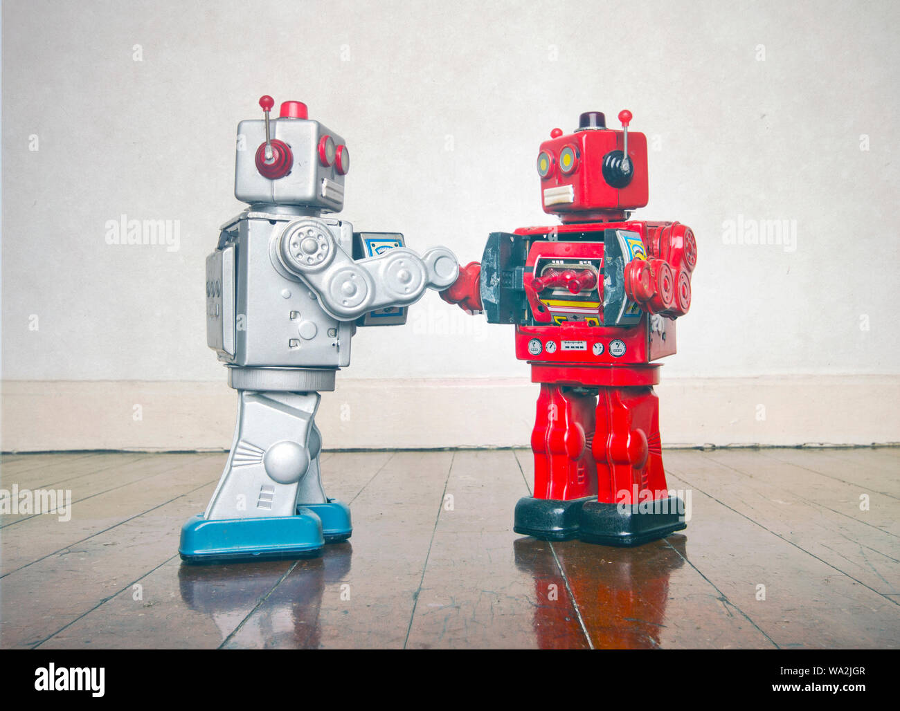 two retro robot toys shake hands on a old wooden floor Stock Photo - Alamy