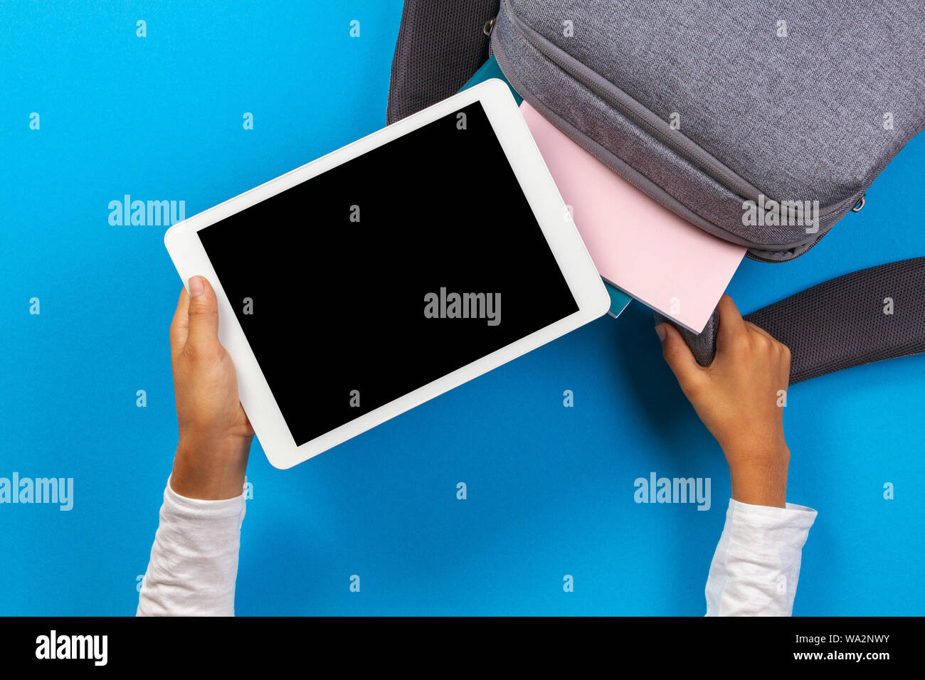 Kid hands taking tablet computer from gray backpack over light blue ...