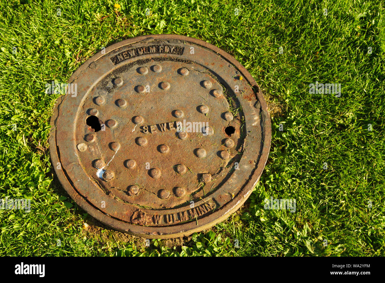 A cast iron sewer manhole cover surround by grass in a city park in ...
