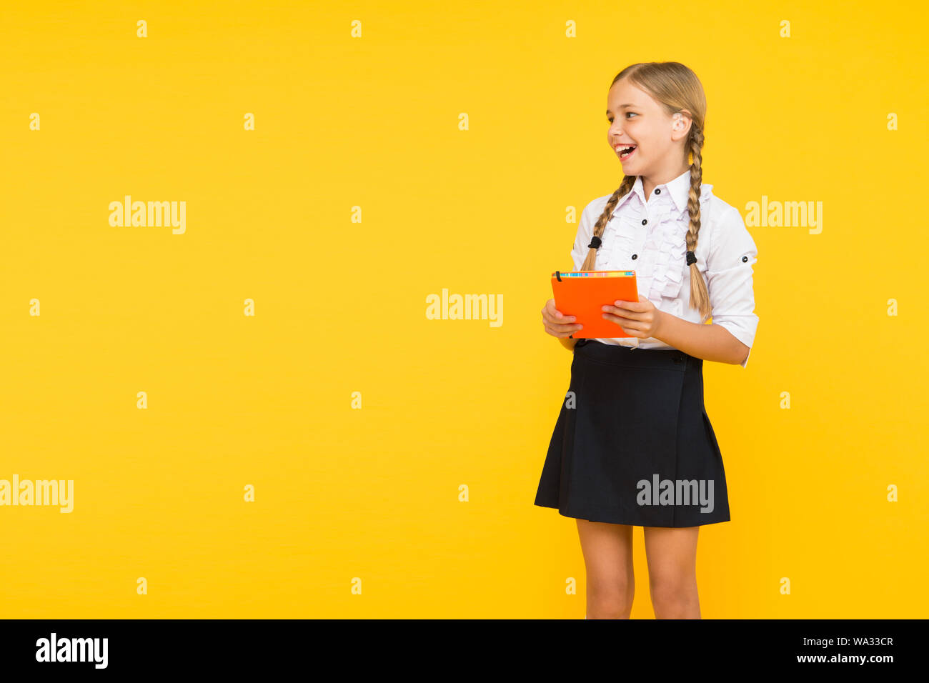 The joy of good knowledge. Cute small girl holding book on yellow ...