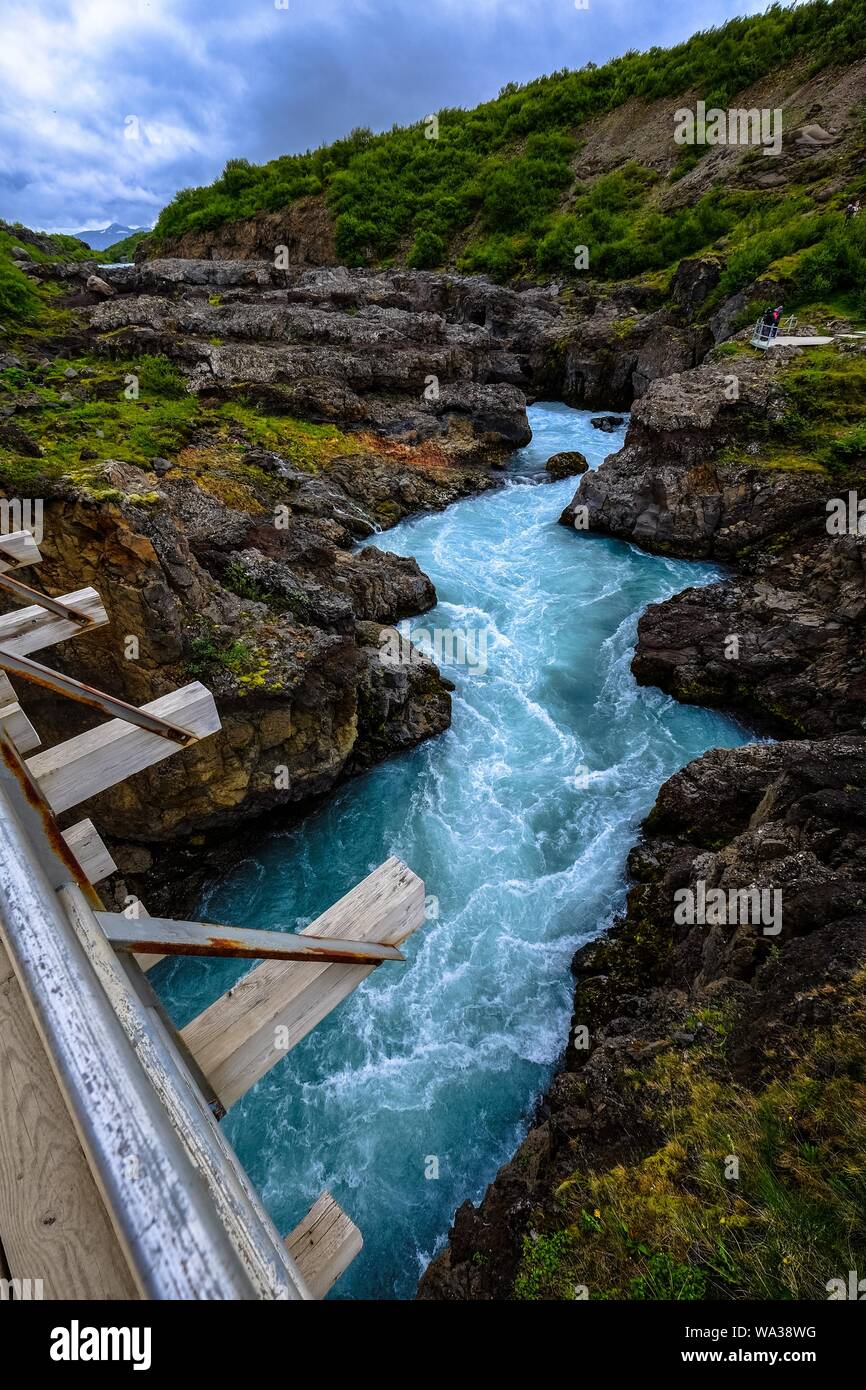 Vertical shot of a river flowing in the middle of cliffs and grassy ...