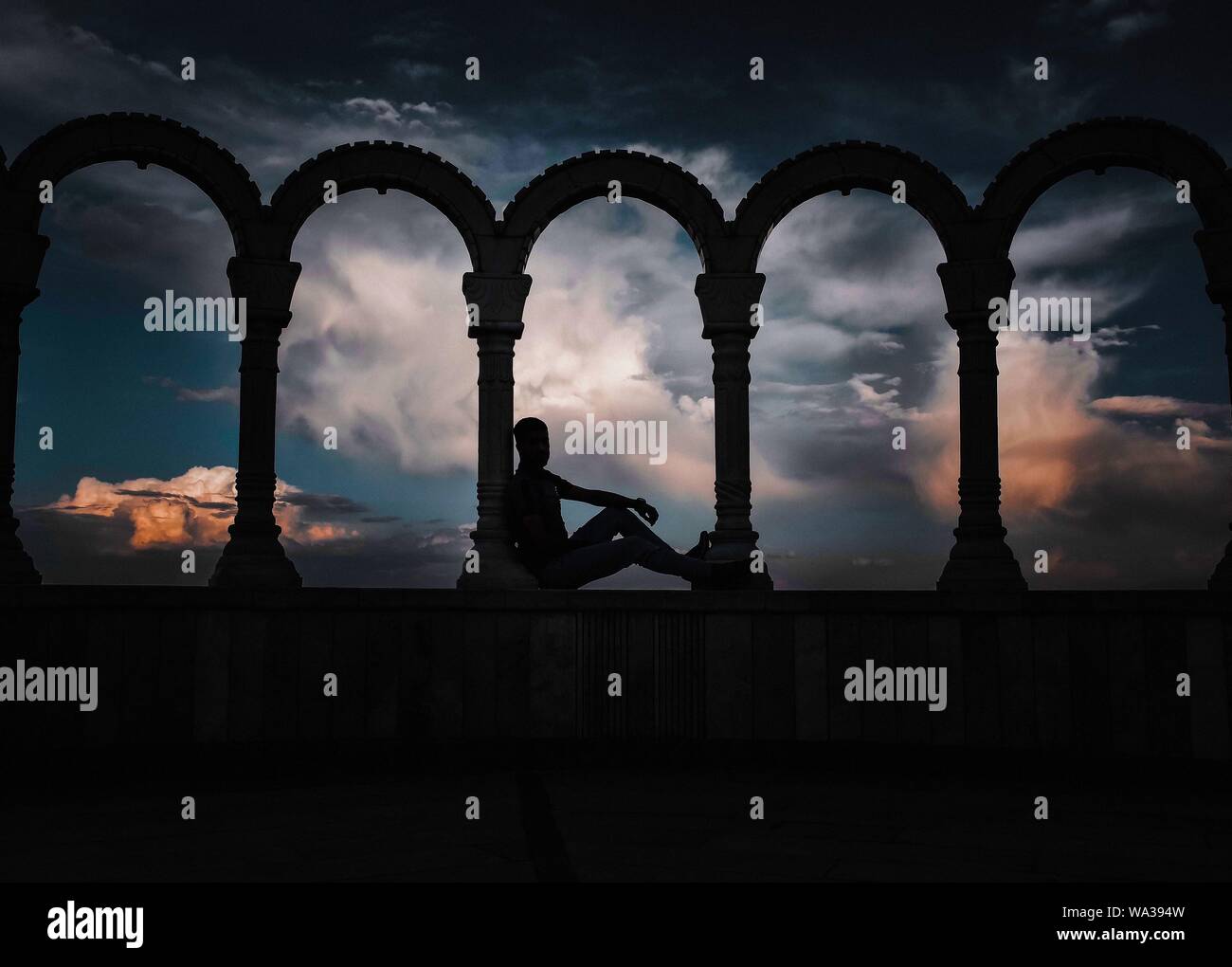 Silhouette of a person sitting on a stone railing and leaning on arch ...
