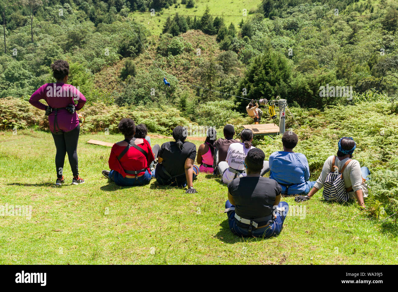 A group of African women sat watching a person on the zip line, The ...