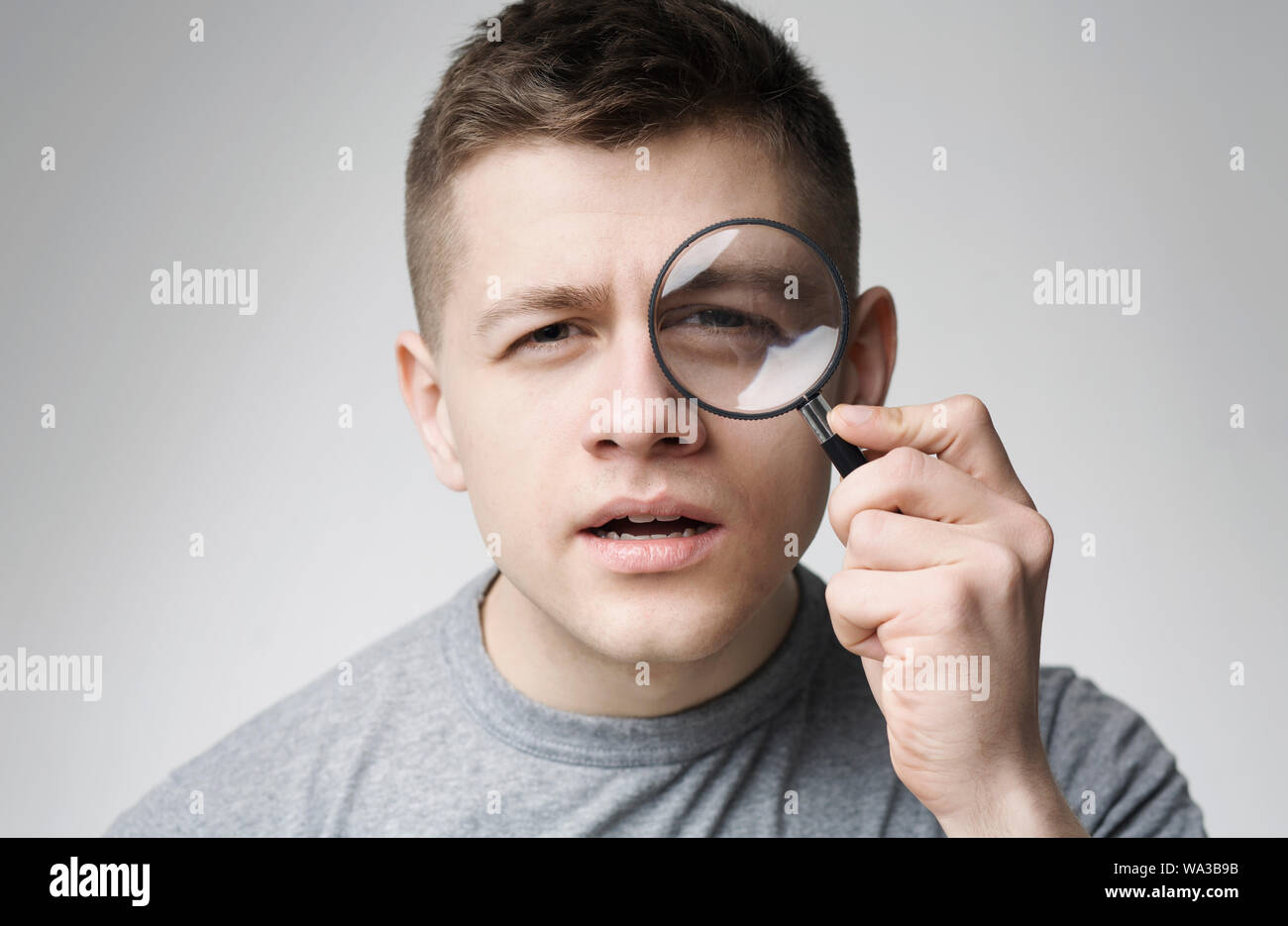 Curious young man looking through magnifying glass Stock Photo - Alamy