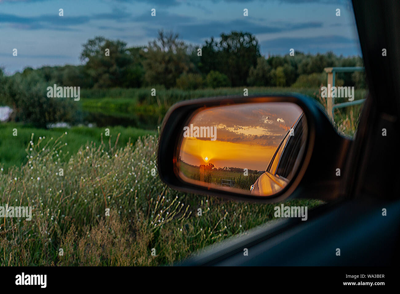 A car´s outside rear view mirror showing a golden sunset over green ... A car´s outside rear view mirror showing a golden sunset over green ...