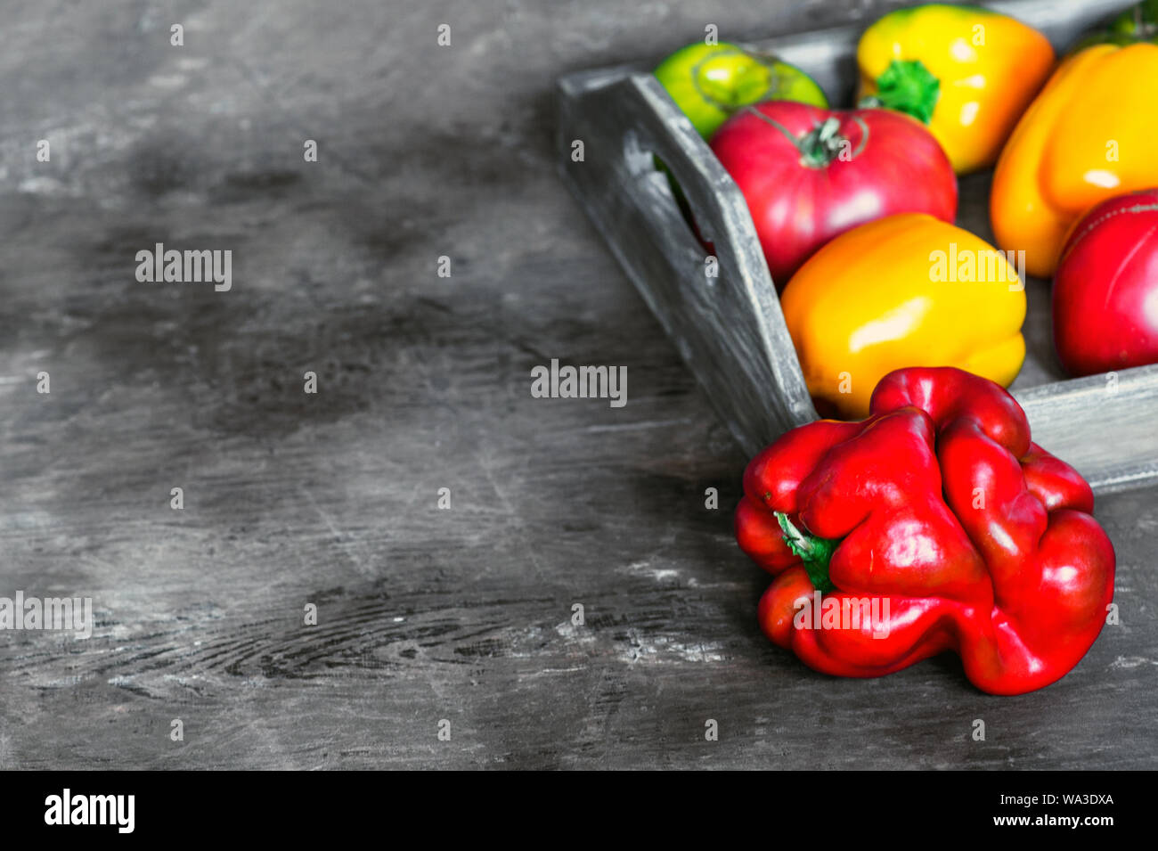 Imperfect natural peppers and tomatoes on an old wooden tray on a dark ...