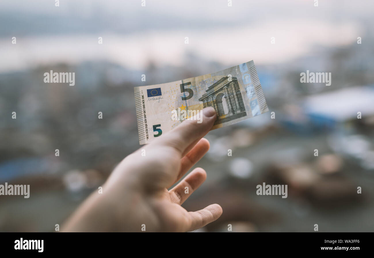 Five euro in hand over city background Stock Photo - Alamy