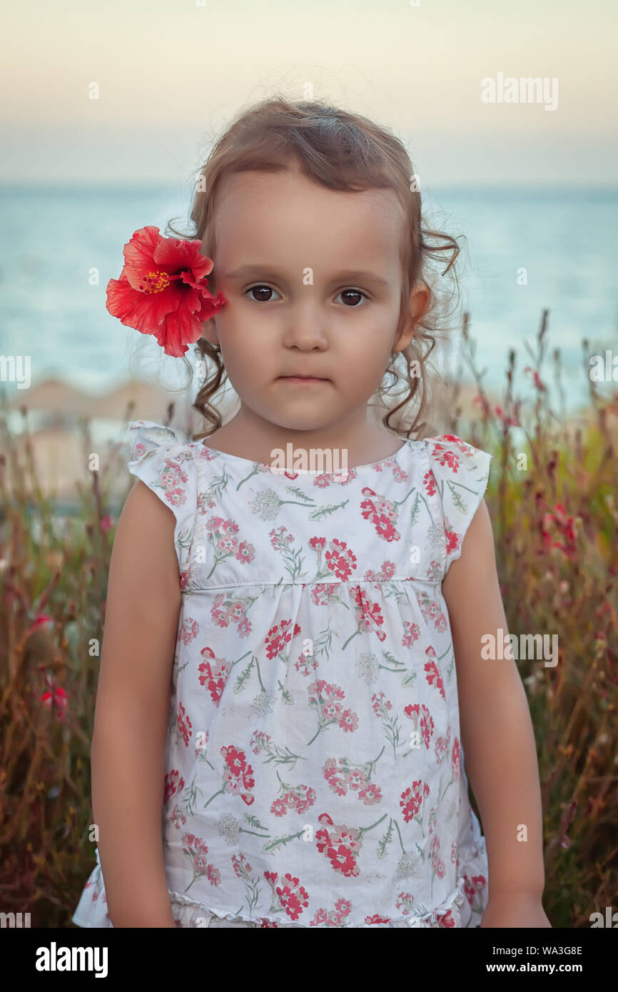 Little child girl with red flower behind her ear Stock Photo - Alamy