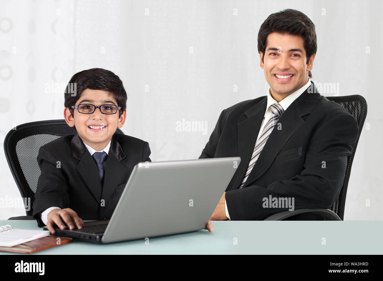 Boy imitating as a businessman and using a laptop with his father Stock ...