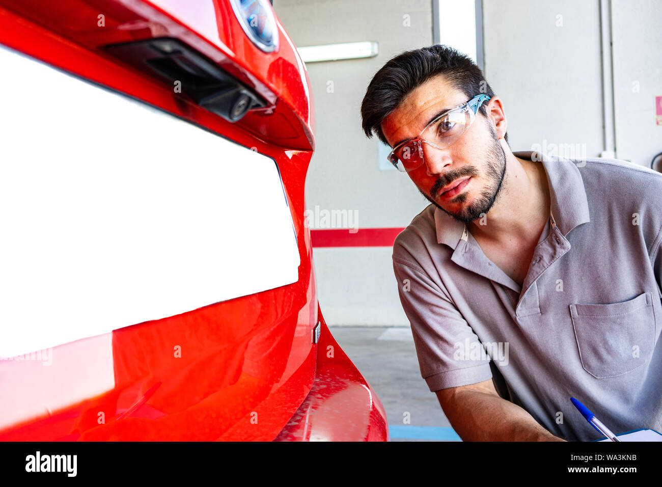 Technician with safety glasses inspecting the rear view camera of a red ...