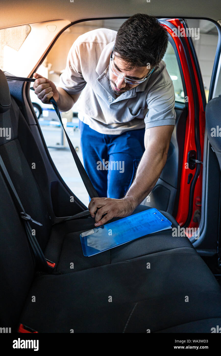 Technician with safety glasses checking the rear seat belts of a red ...