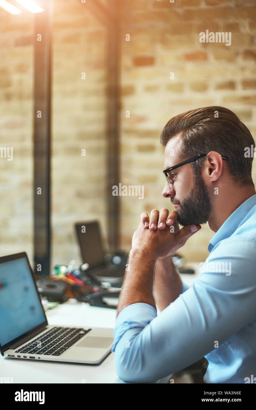Focused on work. Side view of young bearded man in eyeglasses and ...