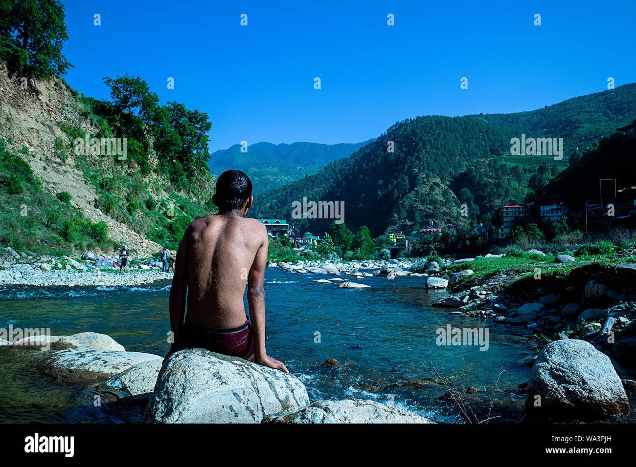 Young boy sitting on a rock near flowing river looking at the beautiful ...