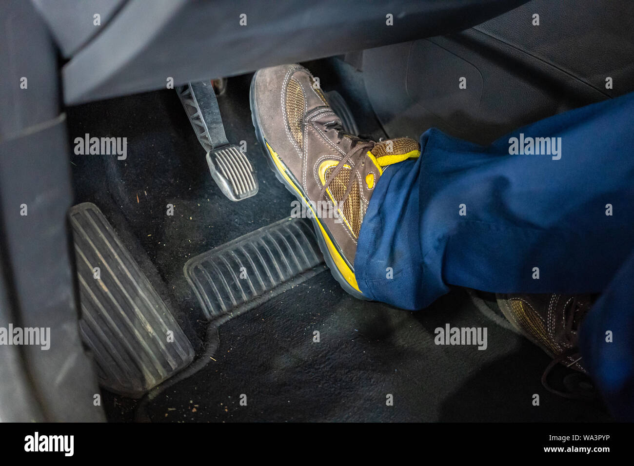 Technician with safety boots testing the brake pedal of a car during a ...