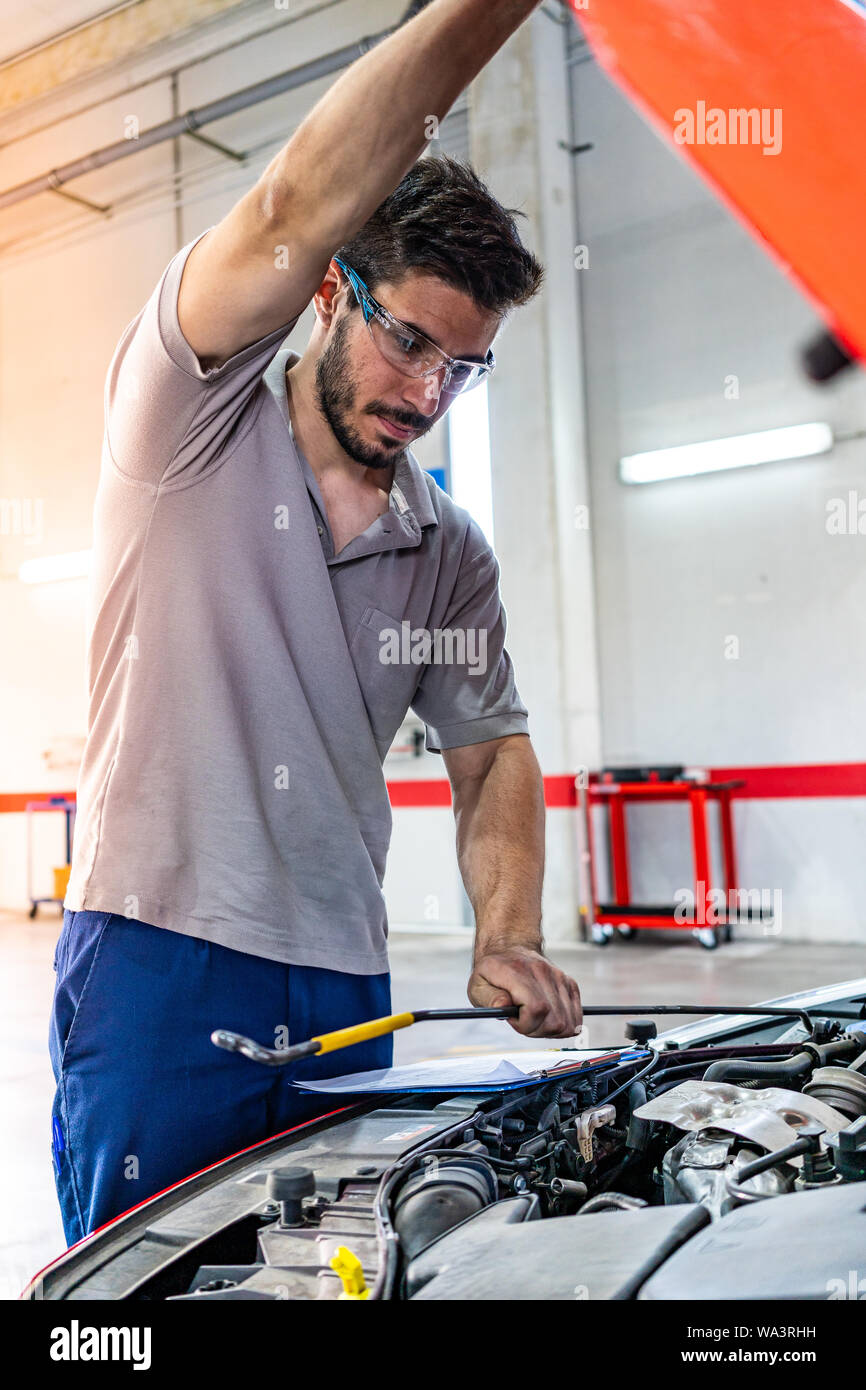 Technician with safety glasses placing the hood support of a red car ...
