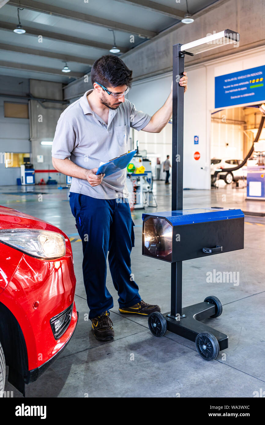 Technician with safety glasses checking the head lights of a red car ...